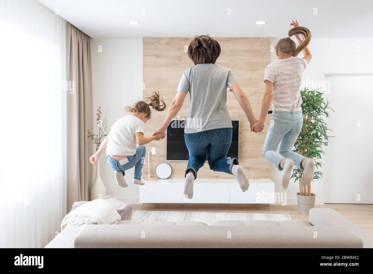 Mother and two daughters having fun jumping on a sofa in living room Stock Photo - Alamy