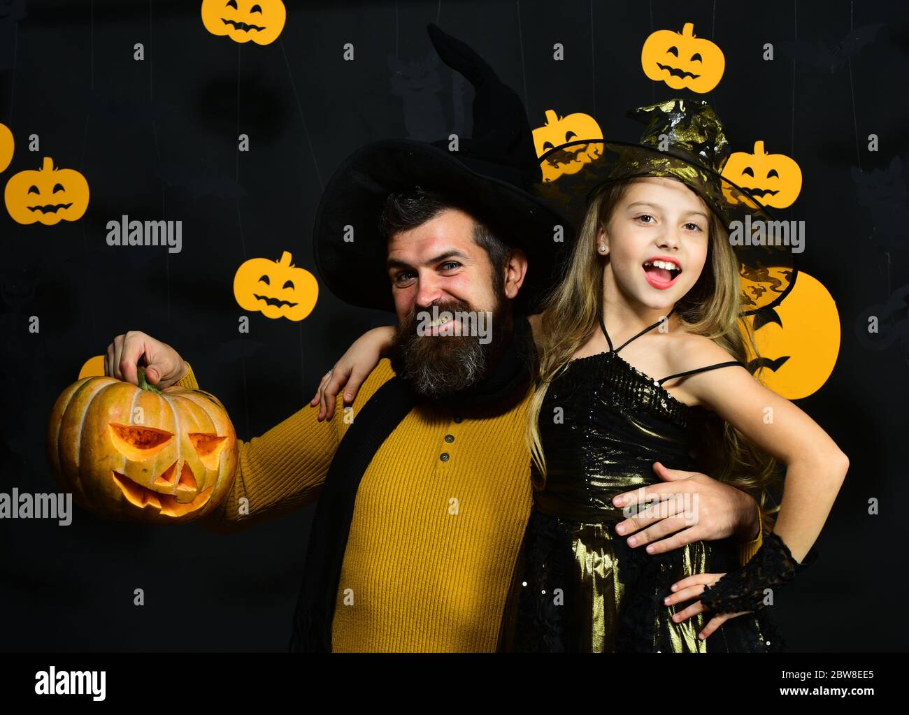 Wizard and little witch in black hats hold pumpkin. Father and daughter ...