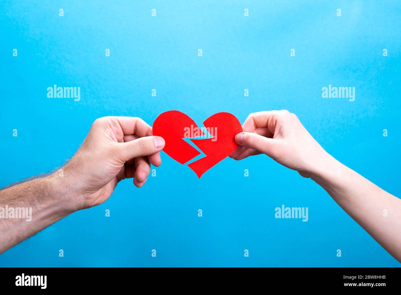 Hands of man and woman tearing a red paper heart on a blue background ...