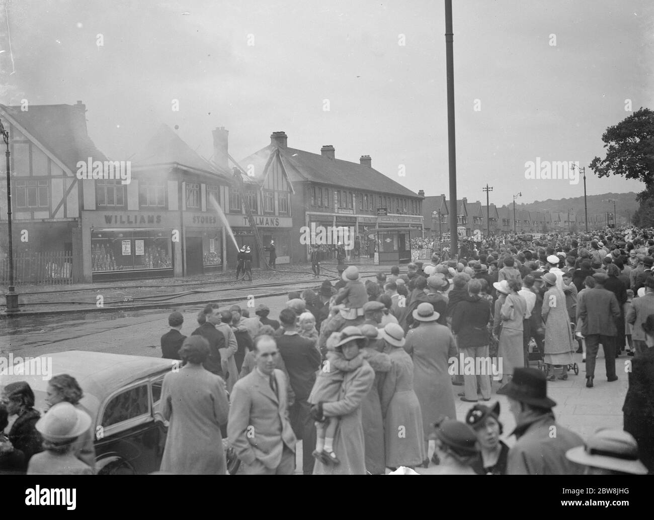 Crowds watch as firemen attempt to put out fires in a parade of shops ...