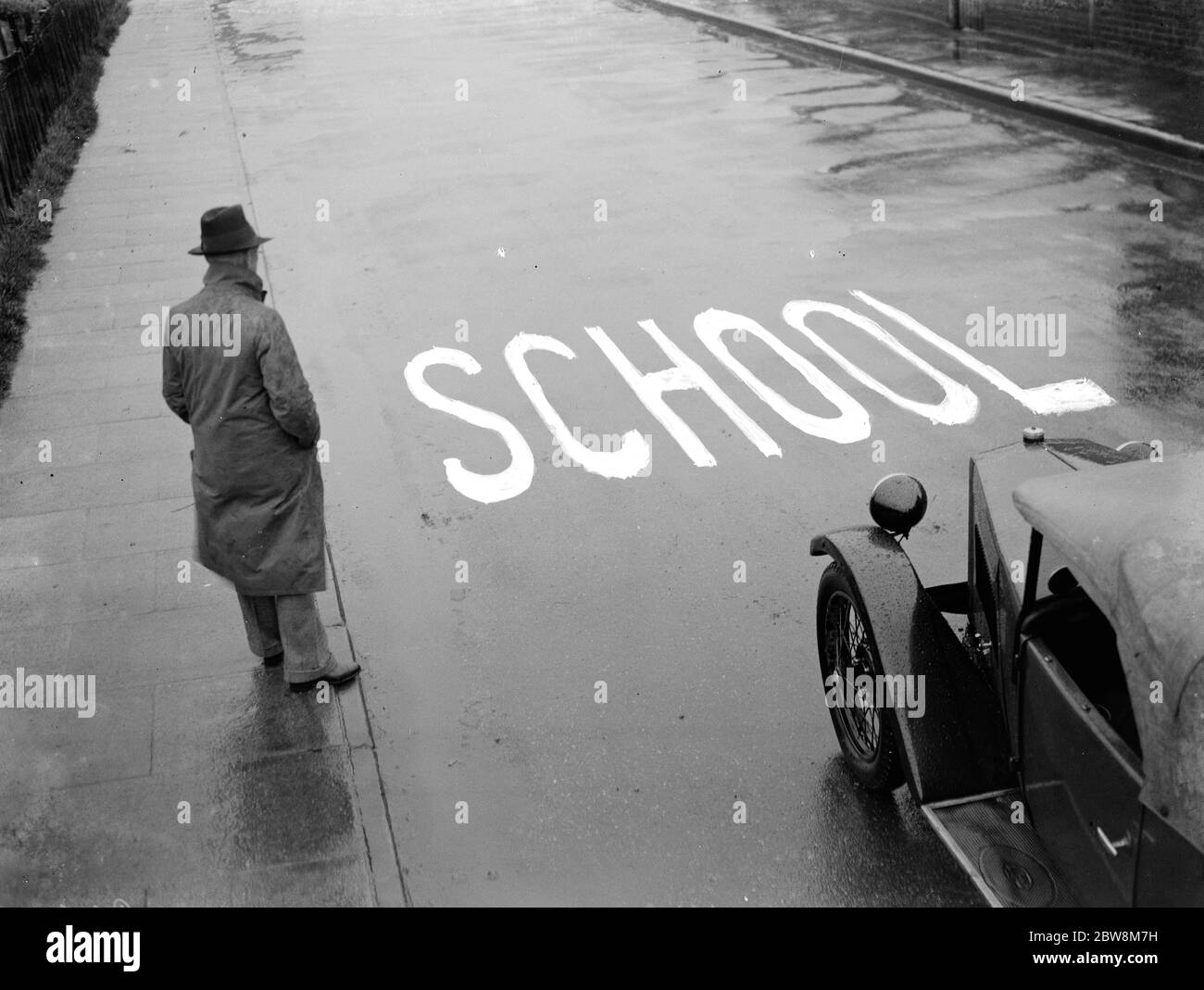 A motorist looks at a painted ' school ' sign on the road . 1935 Stock ...