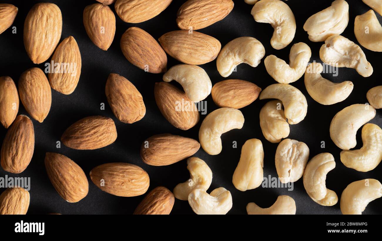 Scattered peeled almond and cashew nuts on black as background, top ...