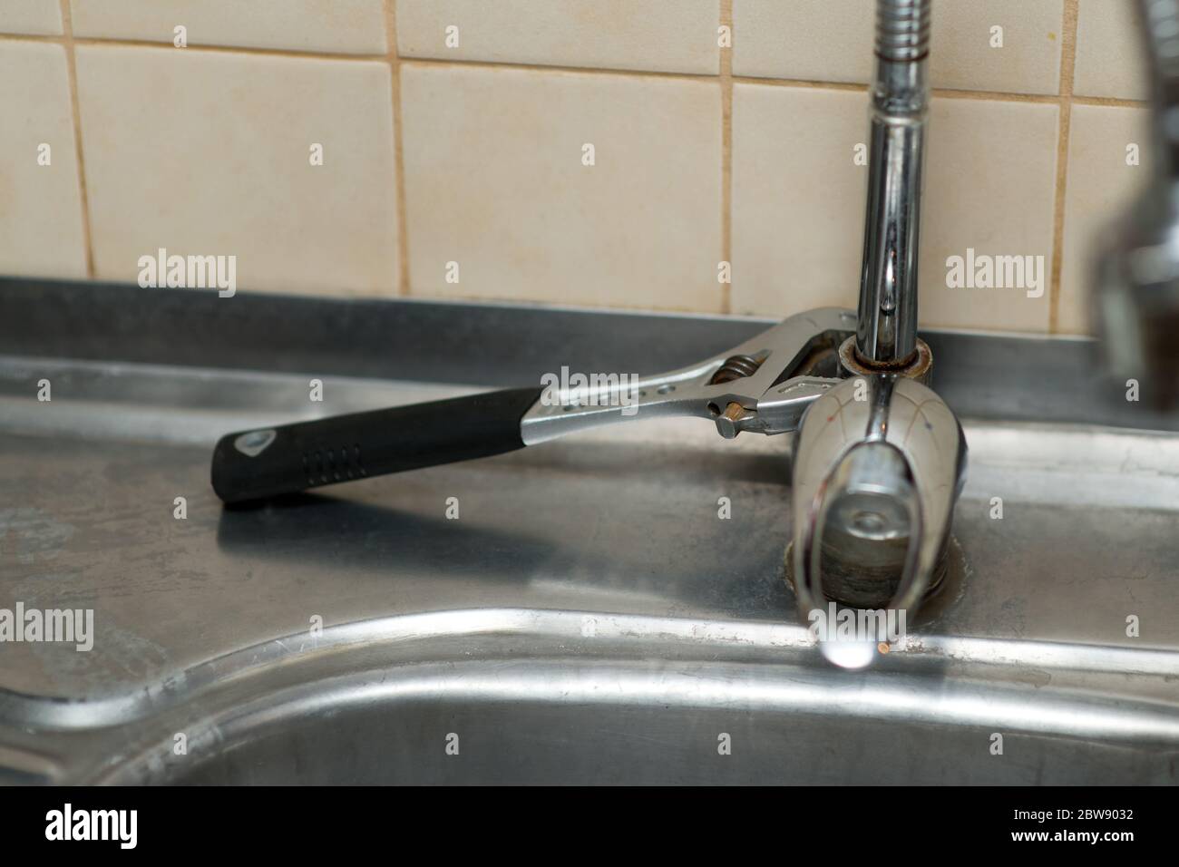 An adjustable spanner lies on a rusty kitchen faucet. Incomplete repair ...