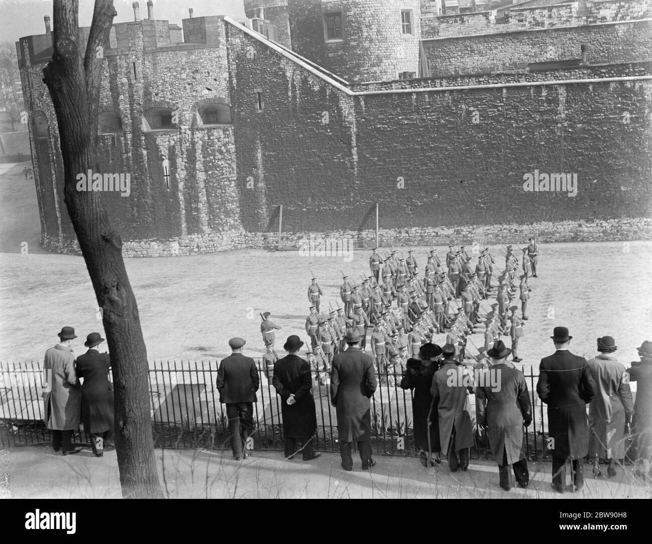 Men looking through railings to the marching soldiers outside the Tower ...