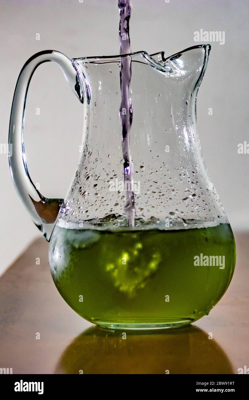 purple liquid being poured into green liquid in a clear glass pitcher ...