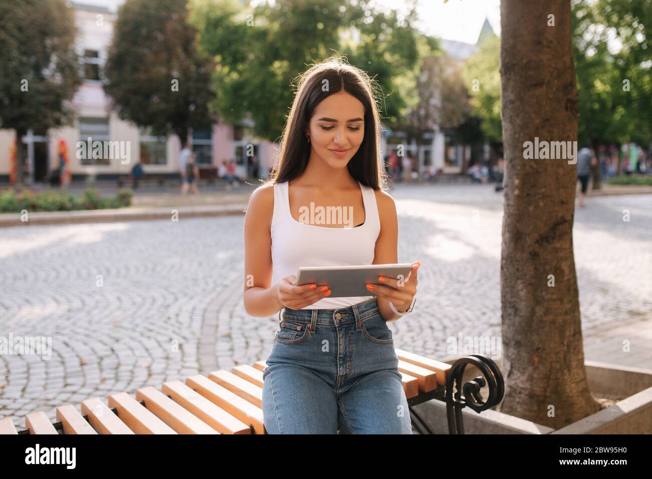 Beautiful girl use tablet outdoors. Female sitting on the bench alone ...