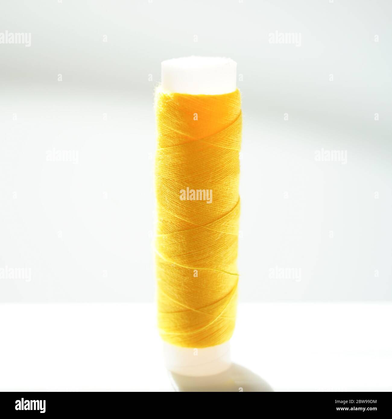 Yellow thread spool on a white bright table, side view Stock Photo - Alamy