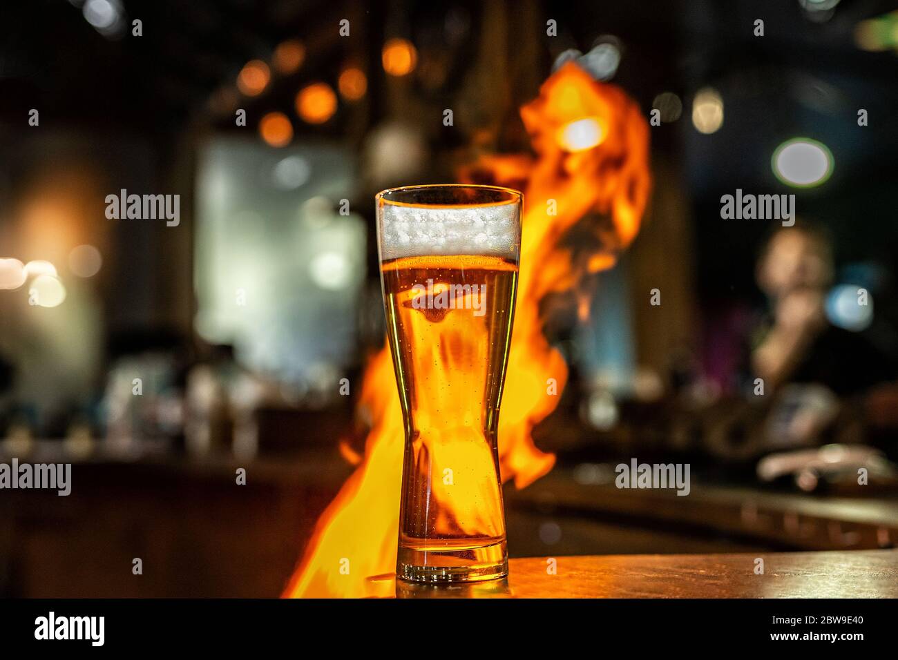 A glass of light lager beer on a background of a burning flame. Amber ...