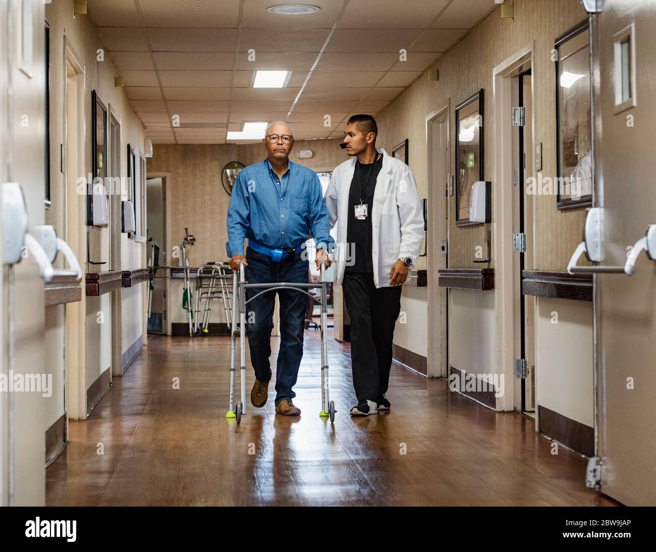 Male nurse assisting senior man walking down corridor with mobility ...