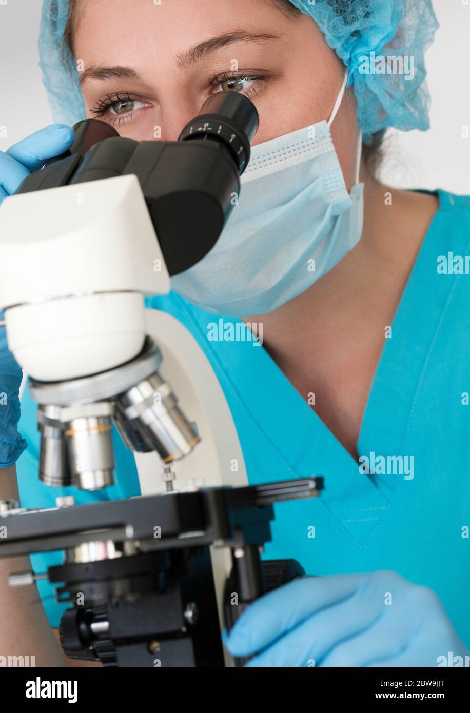 Laboratory technician in face mask looking through microscope Stock ...