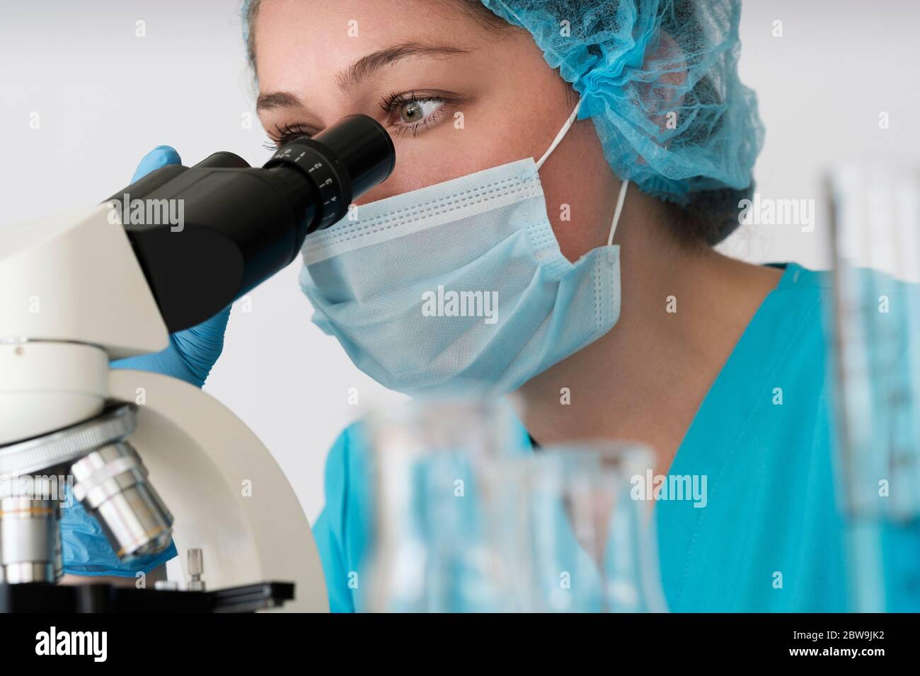 Laboratory technician in face mask looking through microscope Stock ...