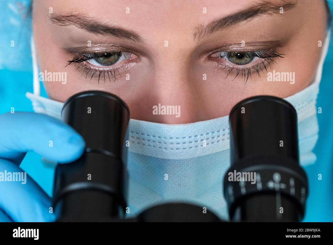 Laboratory technician in face mask looking through microscope Stock ...