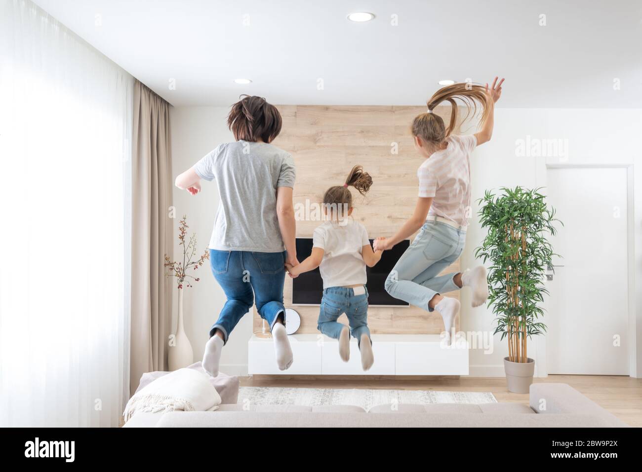 Mother and two daughters having fun jumping on a sofa in living room Stock Photo - Alamy
