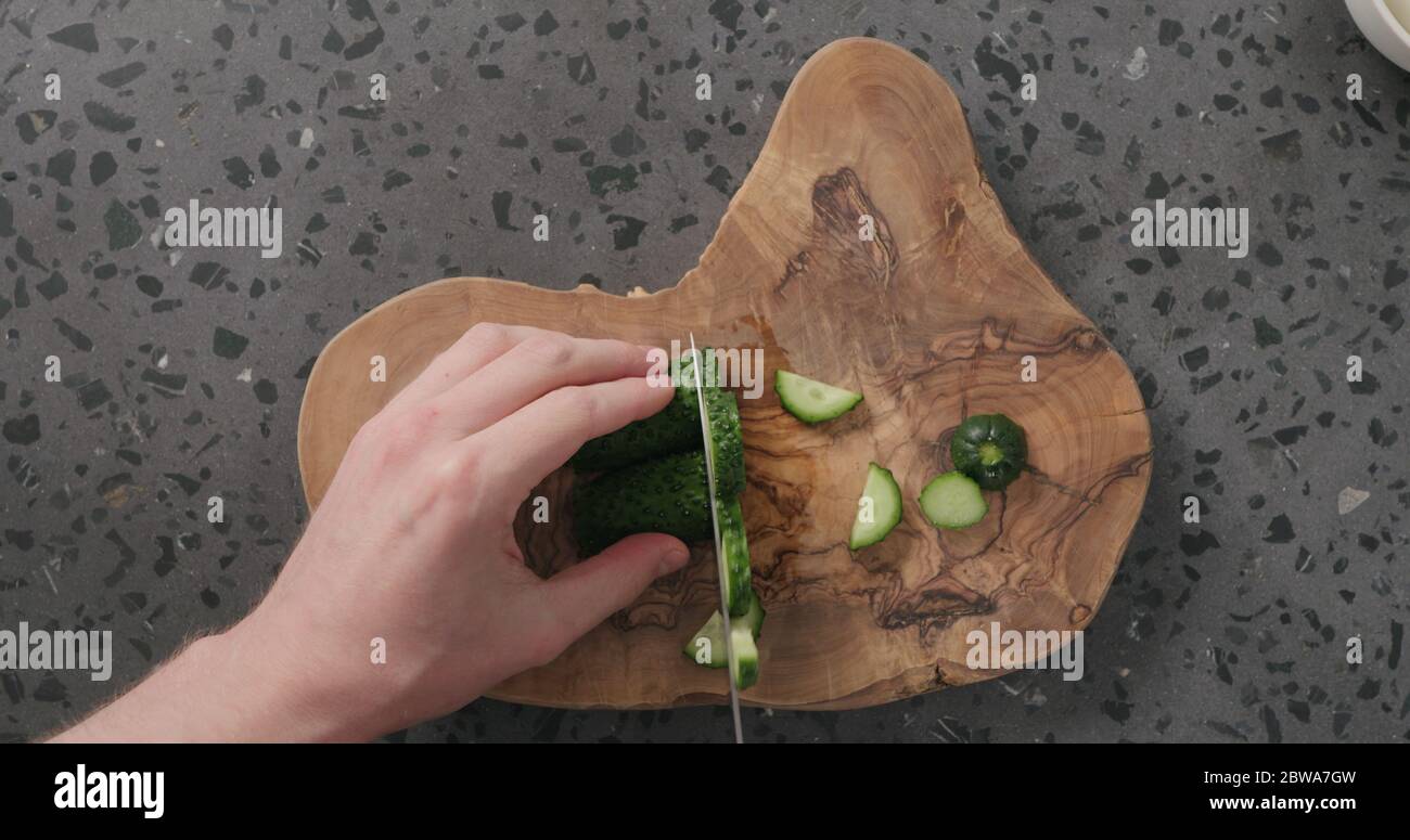Top view man hands cutting fresh cucucmbers on concrete countertop ...