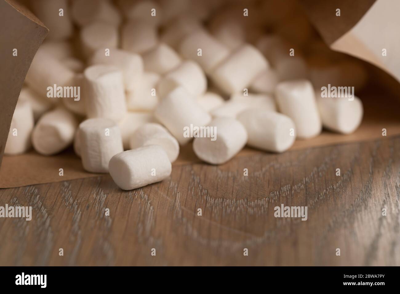small white marshmallows spilling from paper bag on wooden background ...