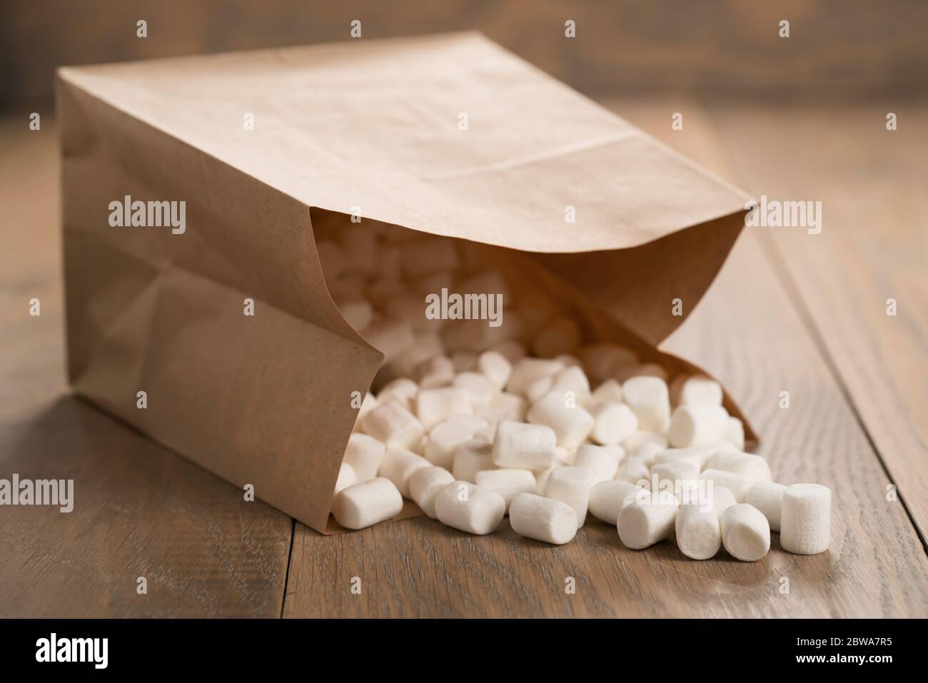 small white marshmallows spilling from paper bag on wooden background ...