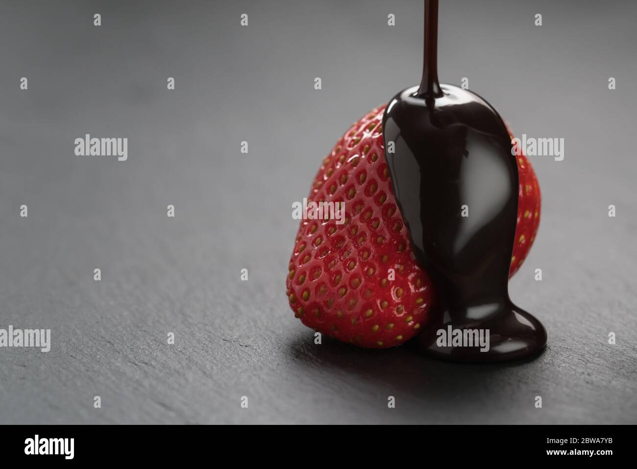 Pour chocolate over ripe strawberry on slate background Stock Photo - Alamy