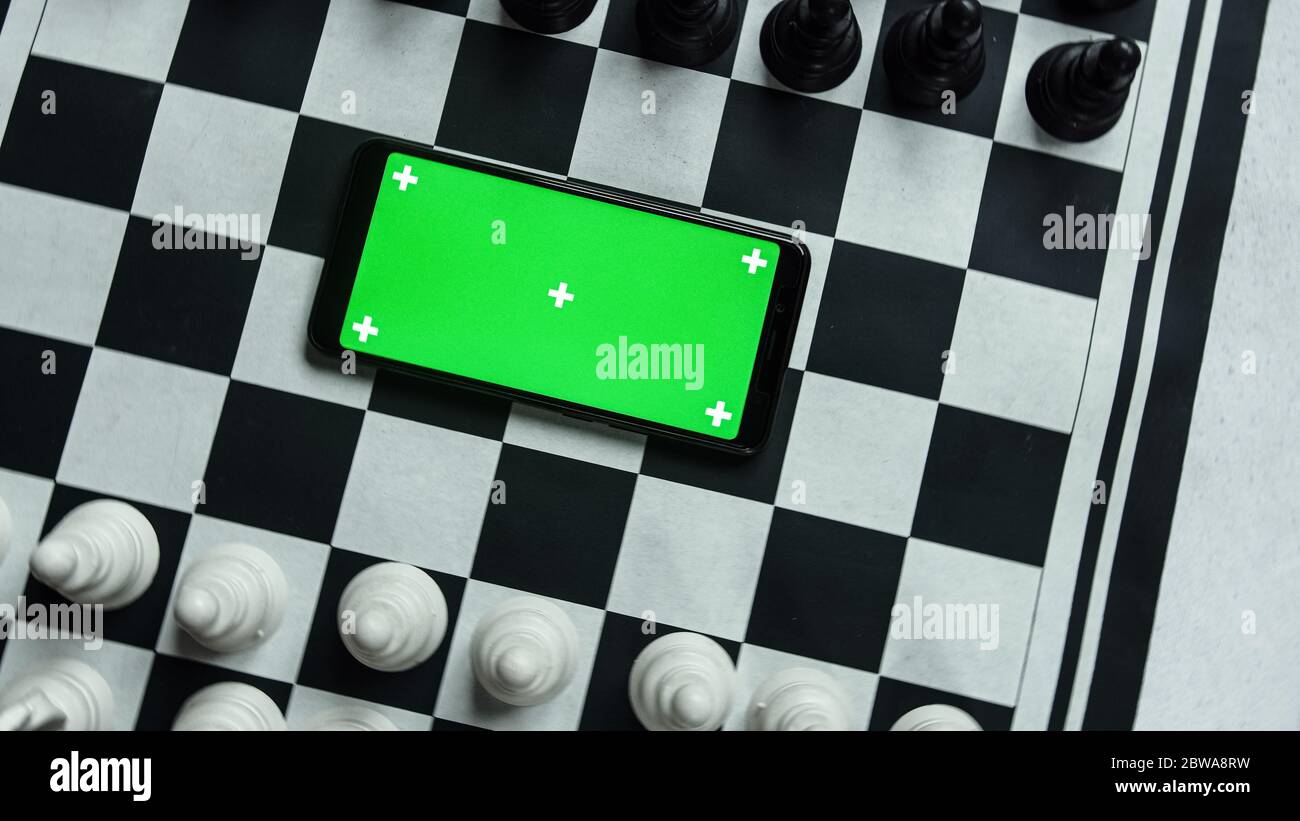 Black and white chess pieces and a smart green screen phone in the ...