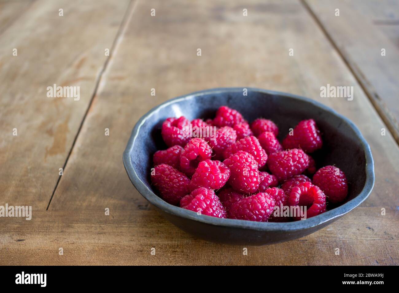 fresh juicy raspberries in handmade black ceramic bowl on wooden plank ...