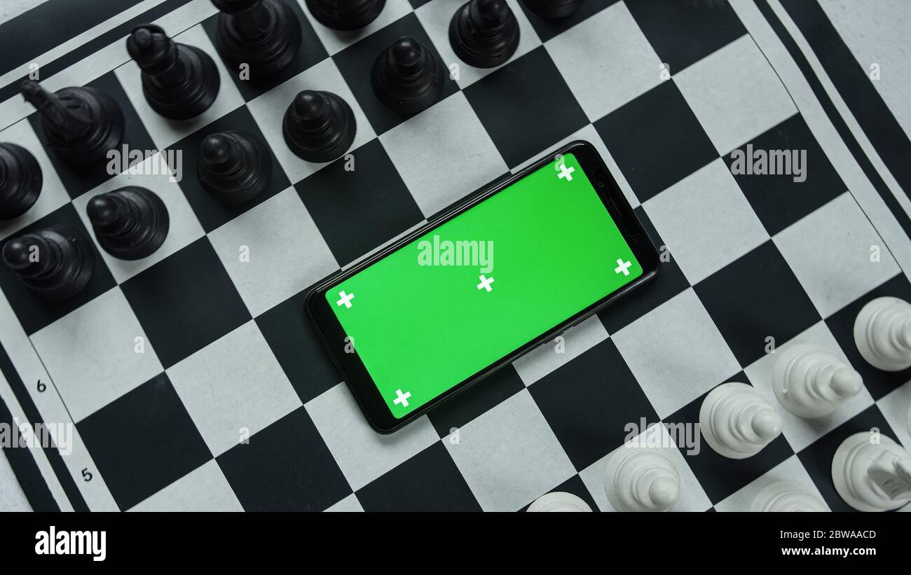 Black and white chess pieces and a smart green screen phone in the ...
