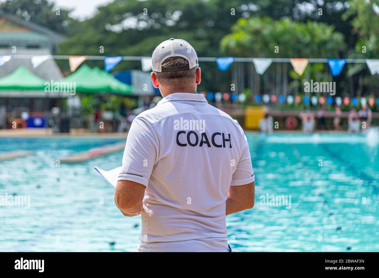 Back of male swimming coach in white coach shirt working at an outdoor ...
