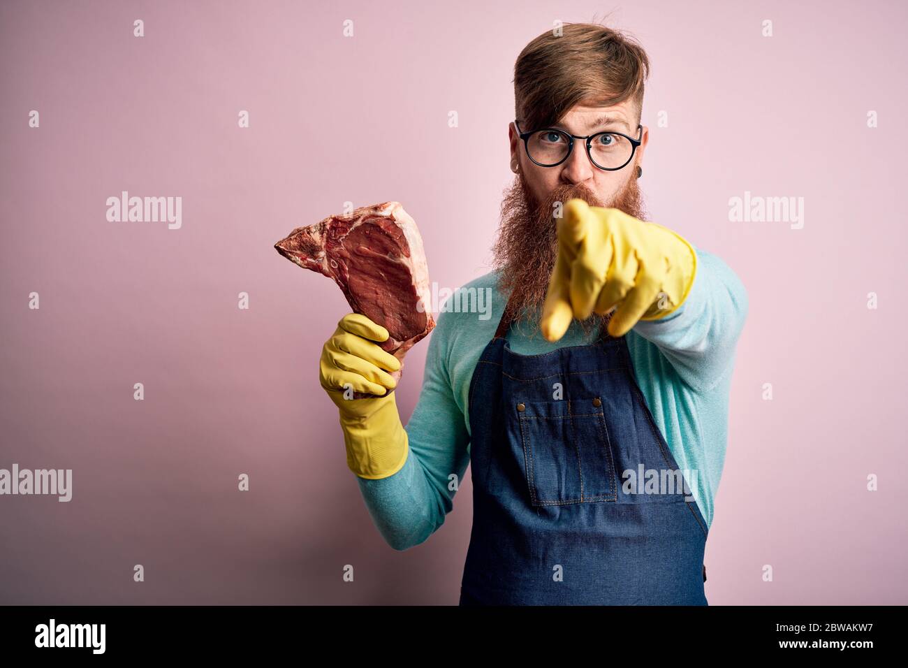 Redhead Irish butcher man with beard holding raw beef steak over pink ...