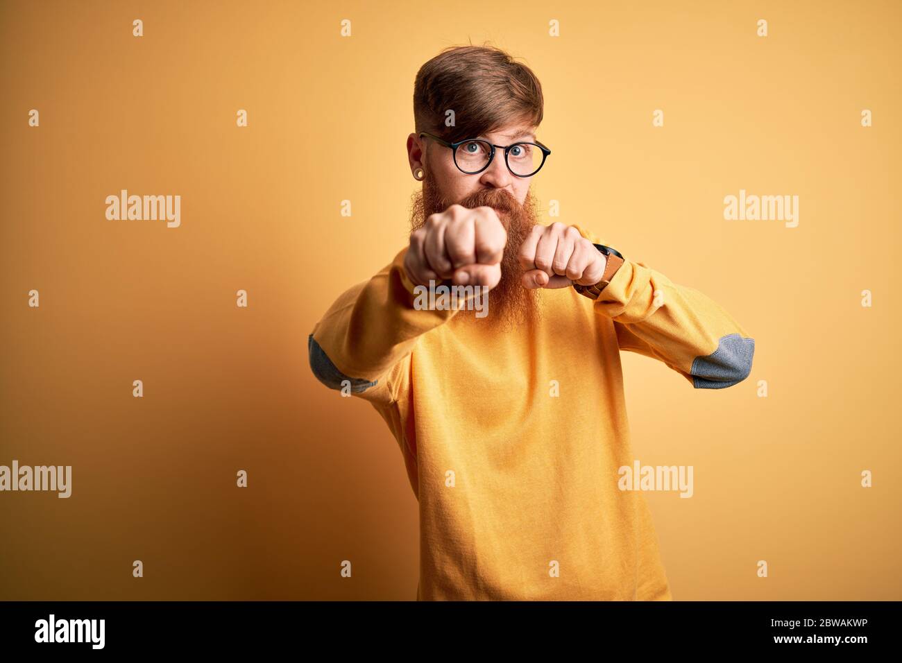 Handsome Irish redhead man with beard wearing glasses over yellow ...