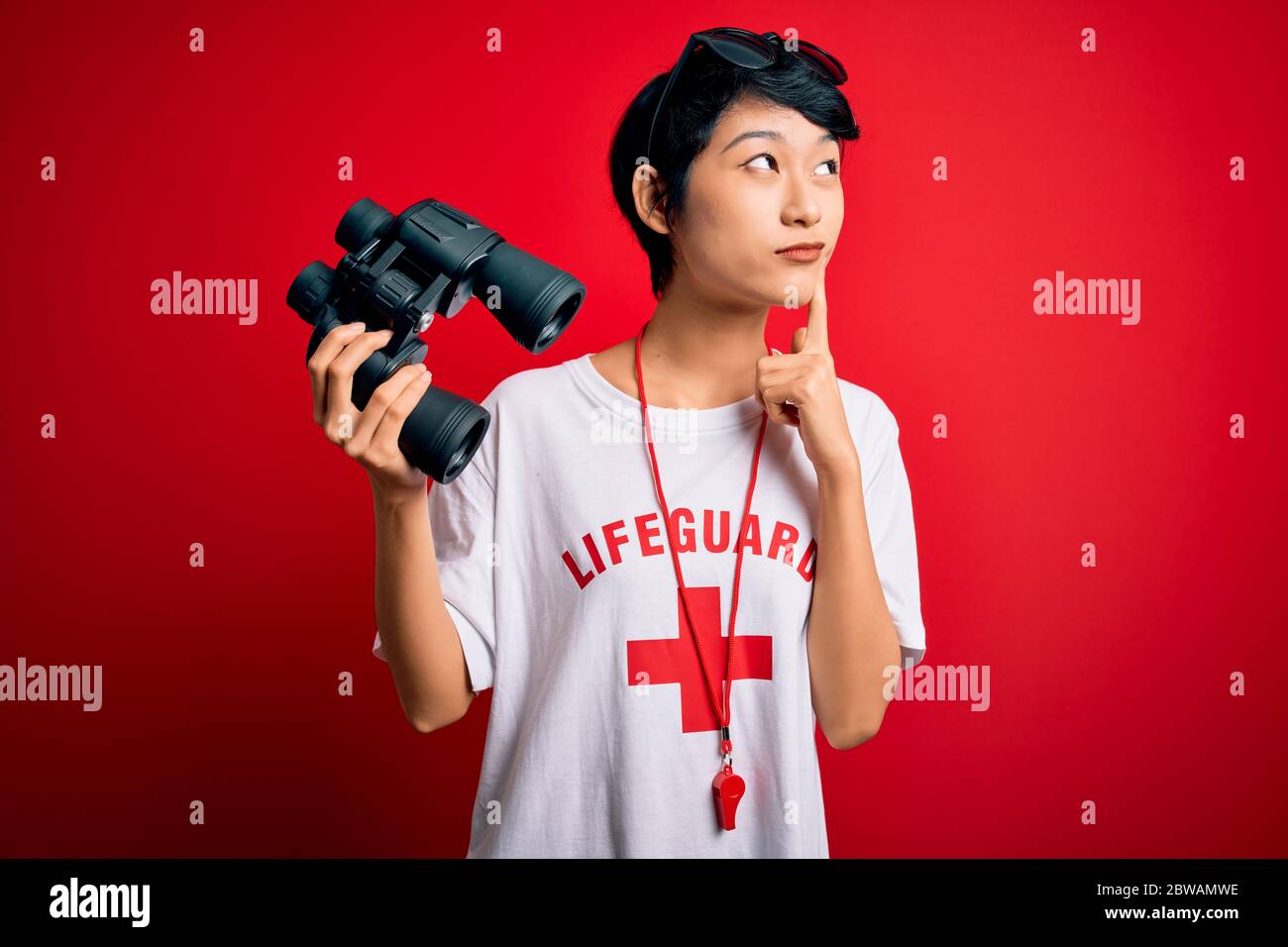 Young beautiful asian lifeguard girl using whistle and binoculars over ...