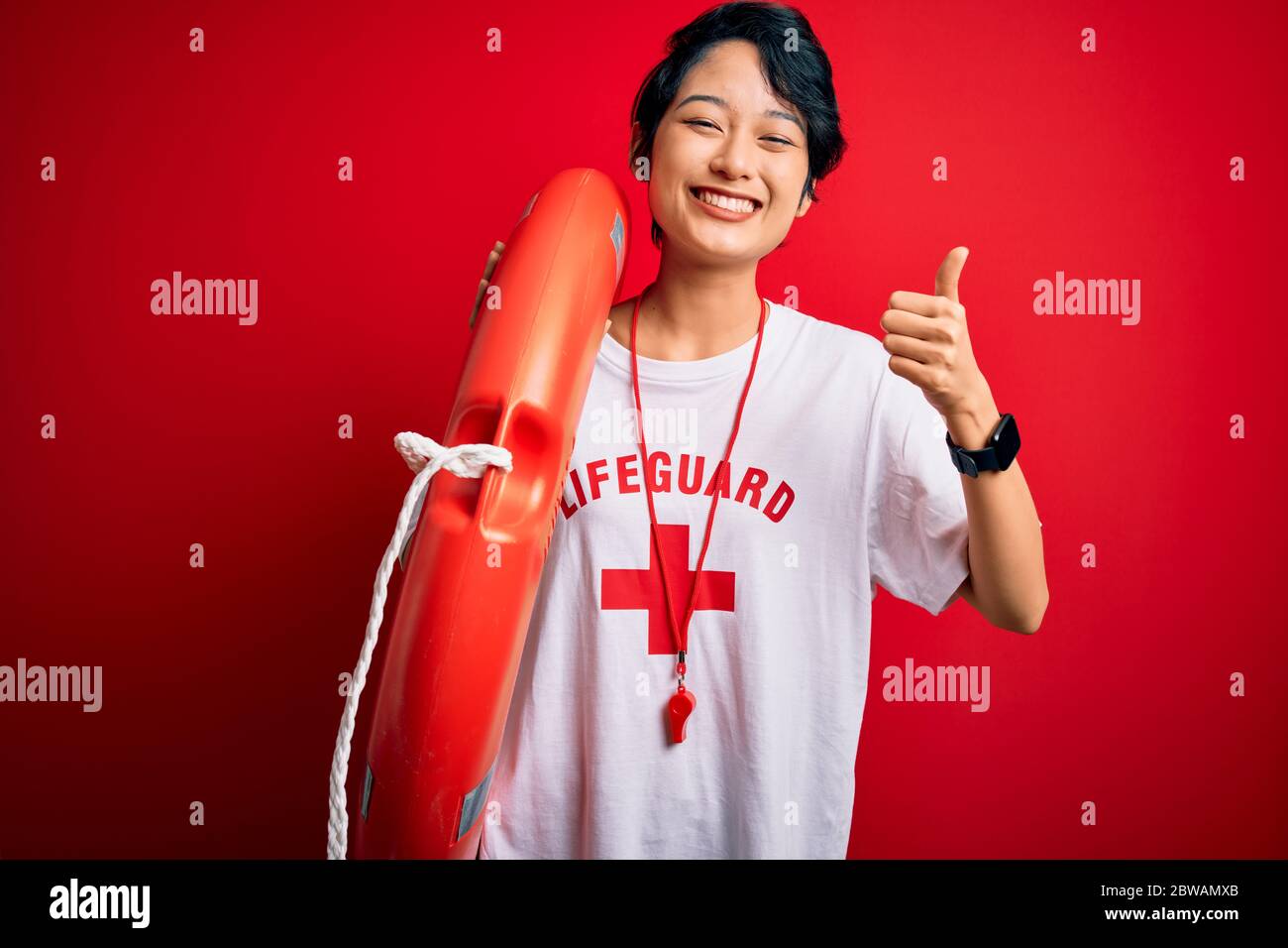 Young beautiful asian lifeguard girl using whistle holding orange float ...