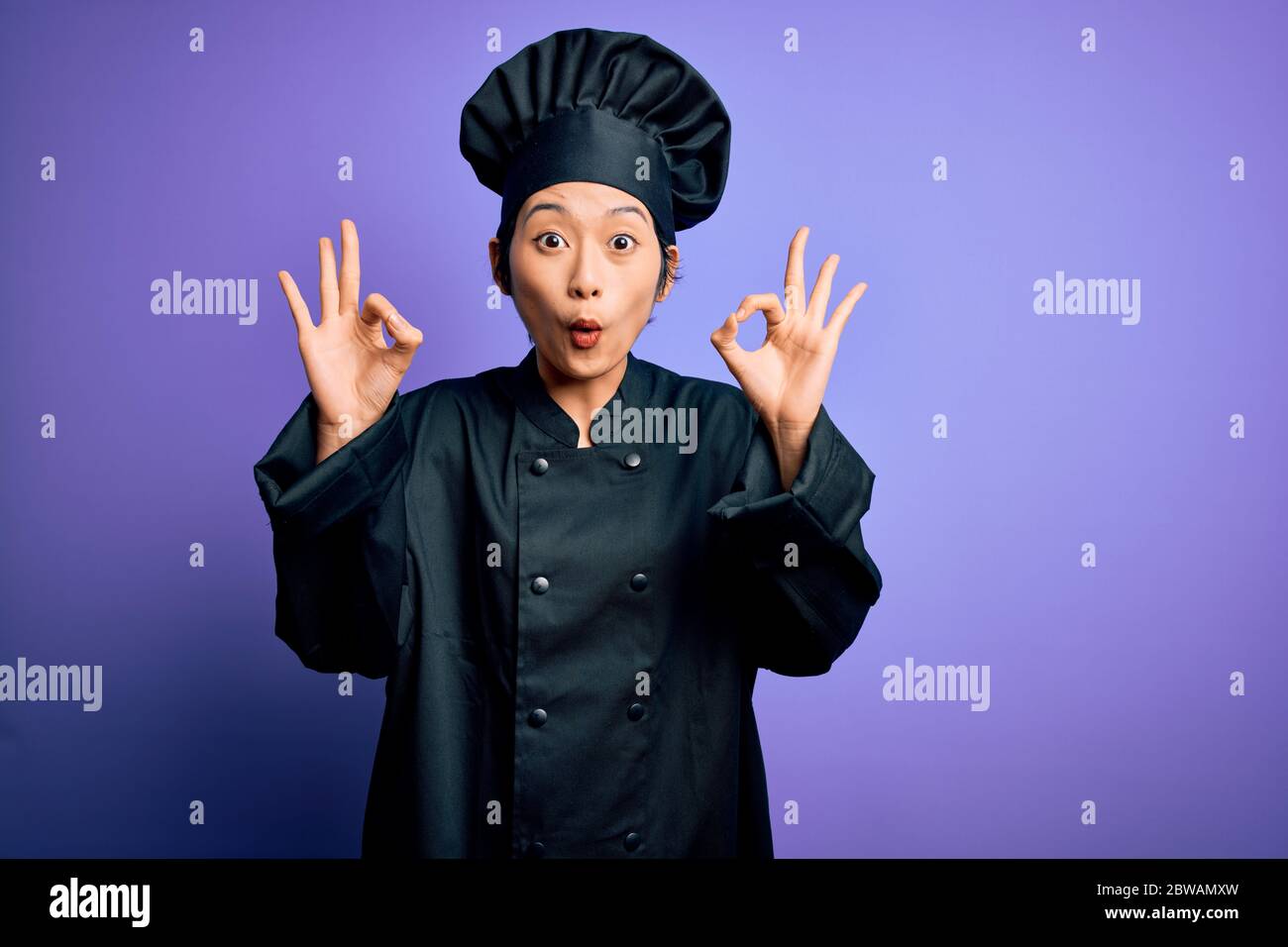 Young beautiful chinese chef woman wearing cooker uniform and hat over ...
