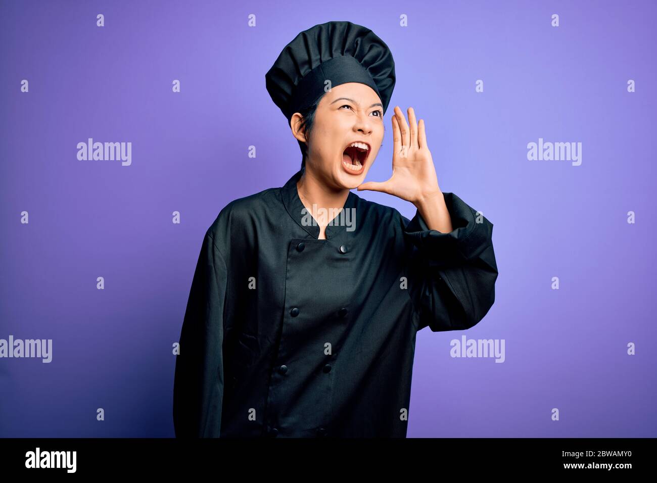Young beautiful chinese chef woman wearing cooker uniform and hat over ...
