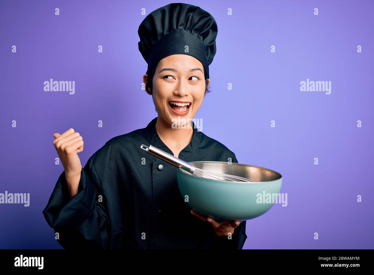 Young beautiful chinese chef woman wearing cooker uniform and hat using ...