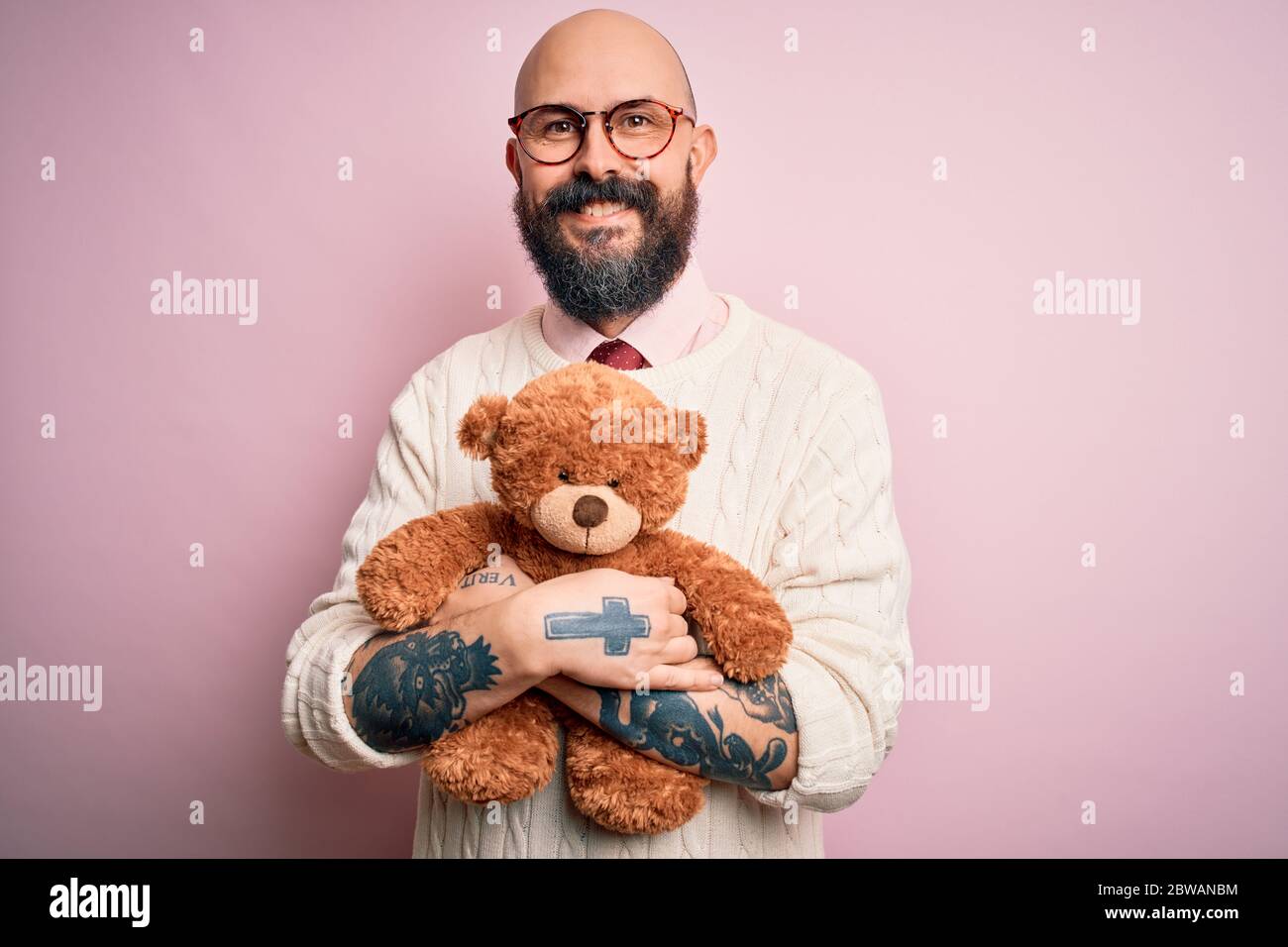 Handsome bald man with beard and tattoo holding teddy bear over ...