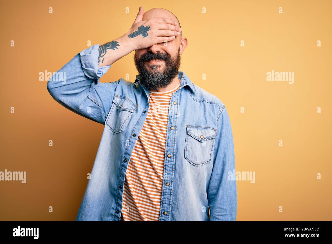 Handsome bald man with beard wearing casual denim jacket and striped t ...