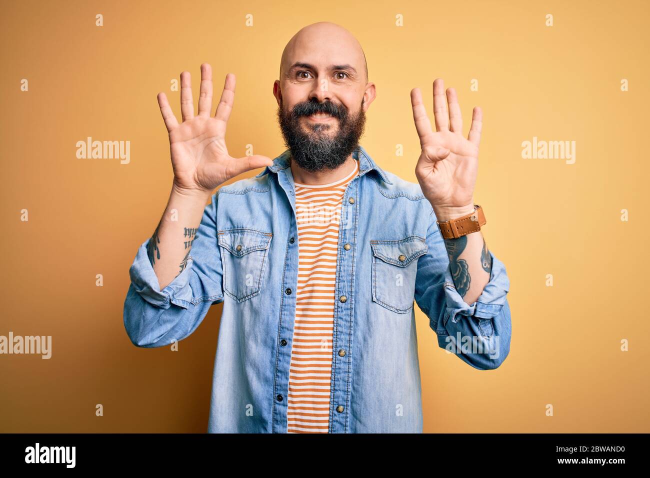 Handsome bald man with beard wearing casual denim jacket and striped t ...