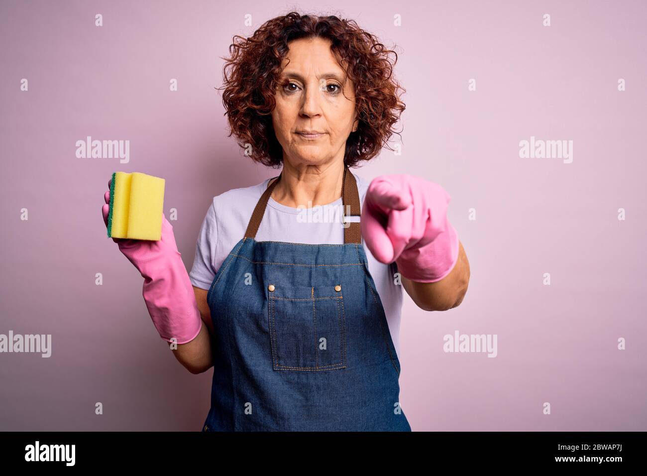 Middle age curly hair woman cleaning doing housework wearing apron and ...