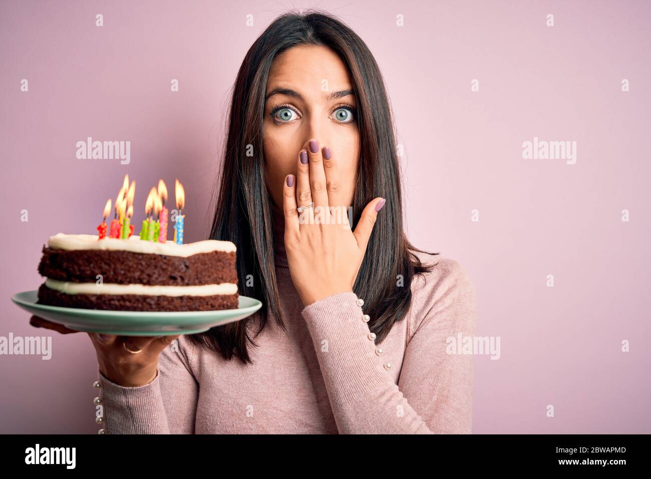 Young woman with blue eyes holding birthday cake with candles over pink ...