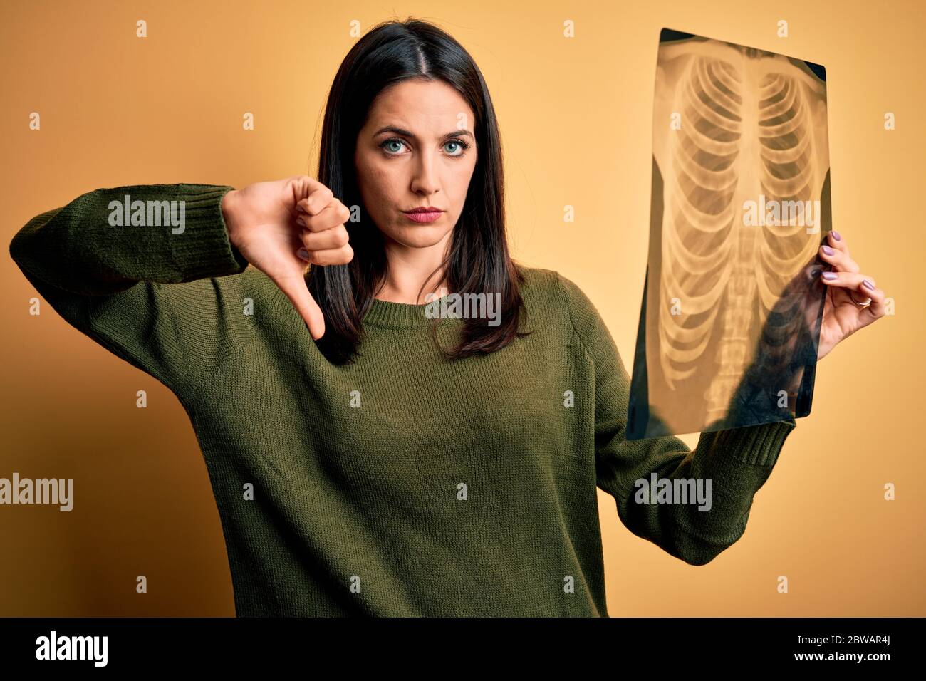 Young brunette woman with blue eyes holding xray of lungs over yellow ...