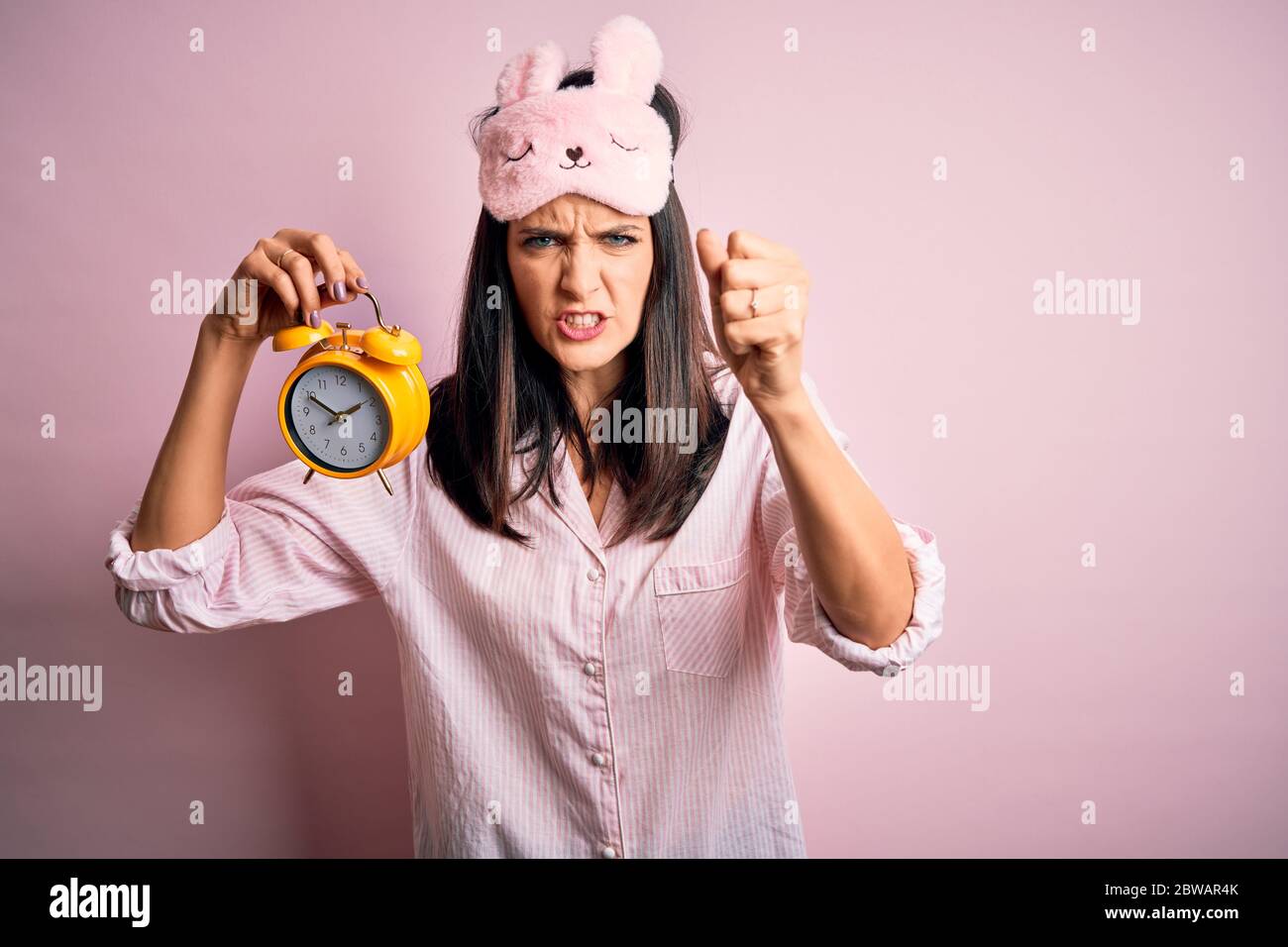 Young brunette woman with blue eyes wearing pajama and eye mask holding ...