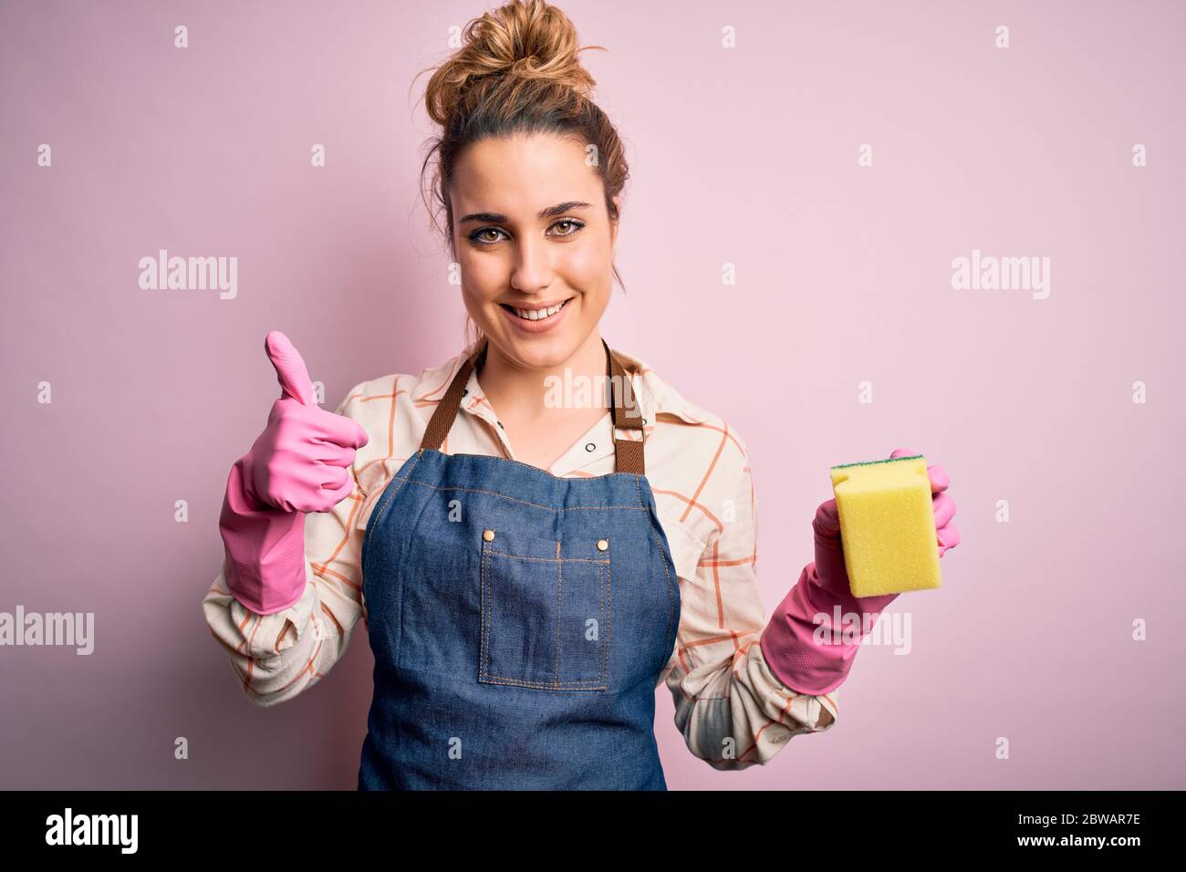Beautiful blonde cleaner woman doing housework wearing arpon and gloves ...