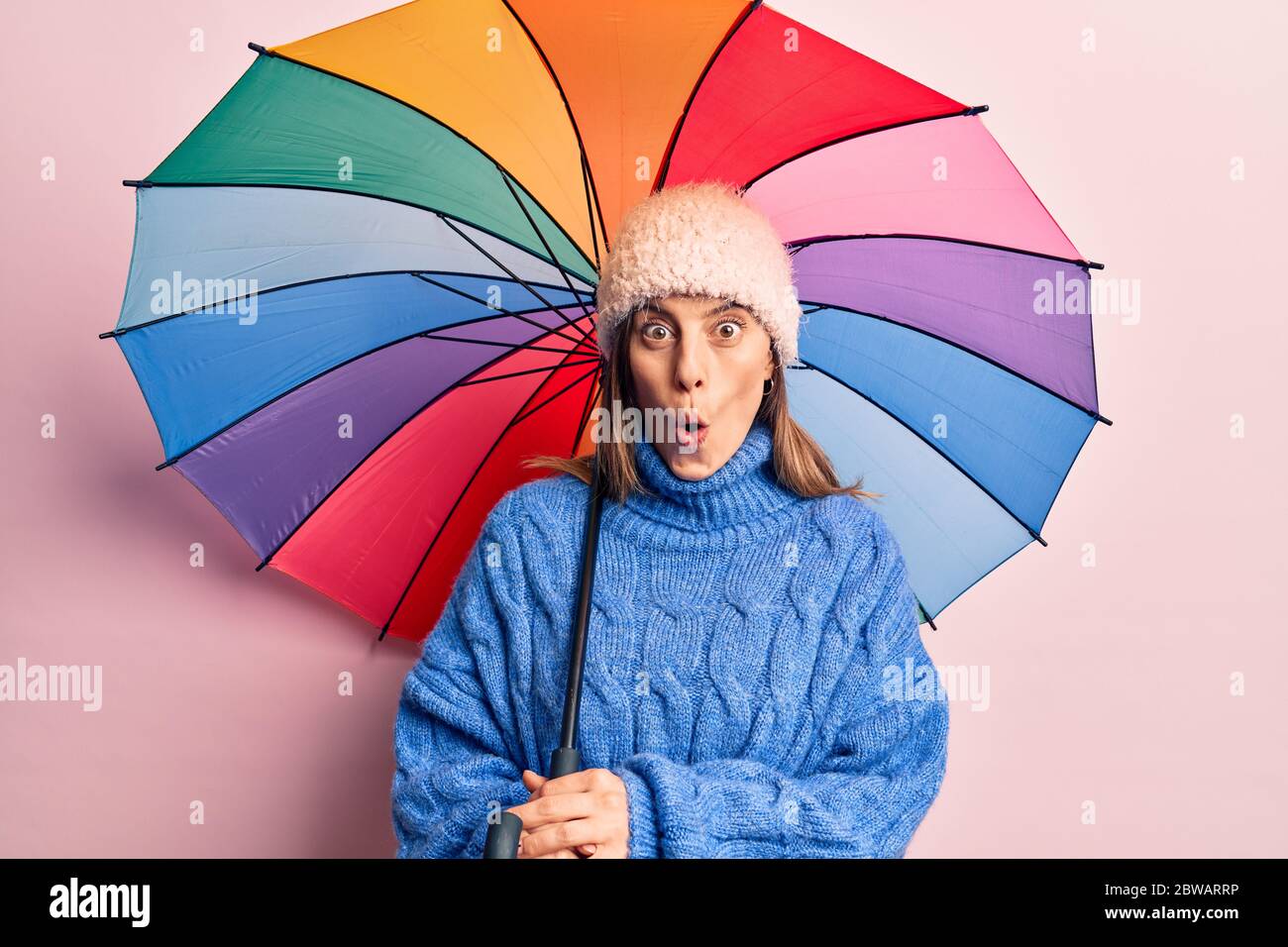 Young beautiful woman holding colorful umbrella scared and amazed with ...