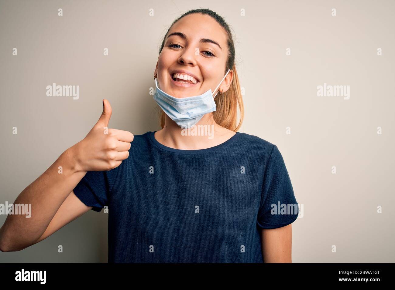 Beautiful blonde woman with blue eyes wearing medical mask over white ...