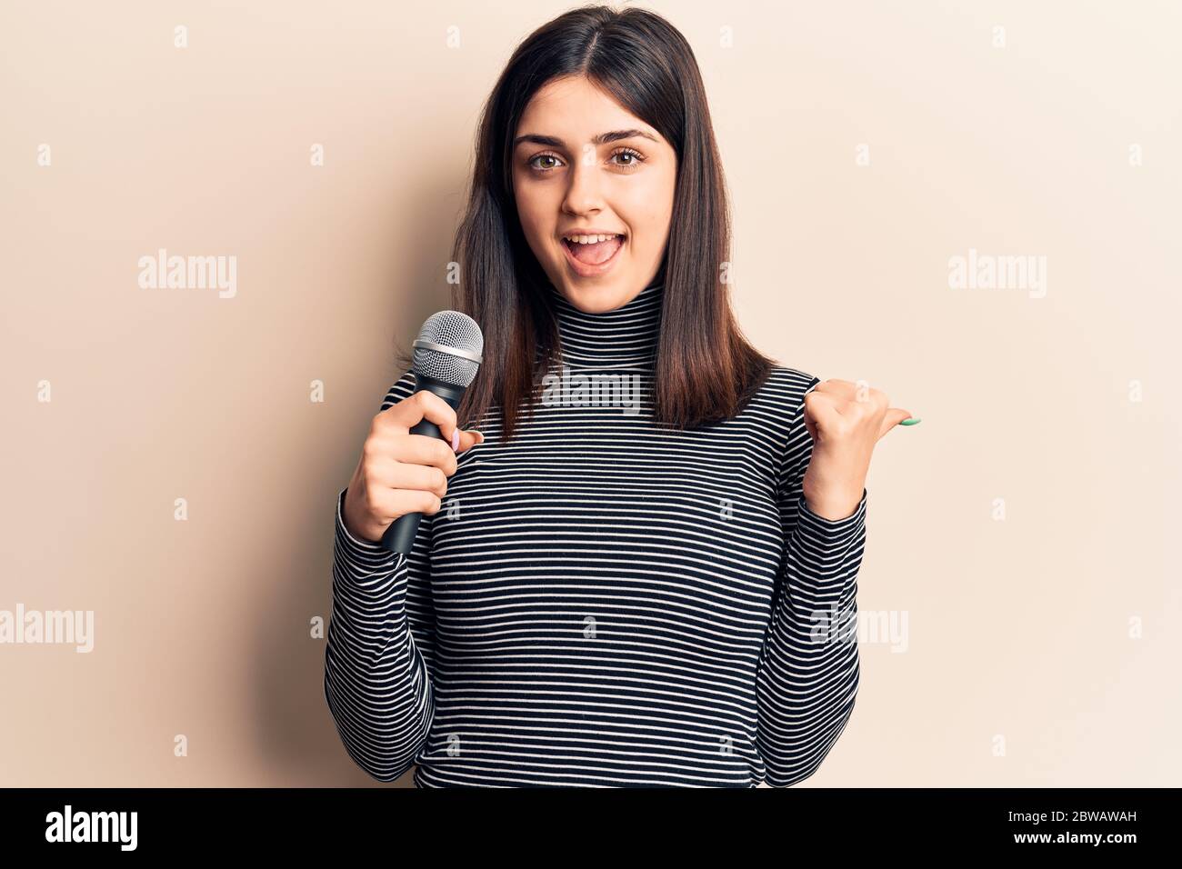 Young beautiful girl singing song using microphone pointing thumb up to ...