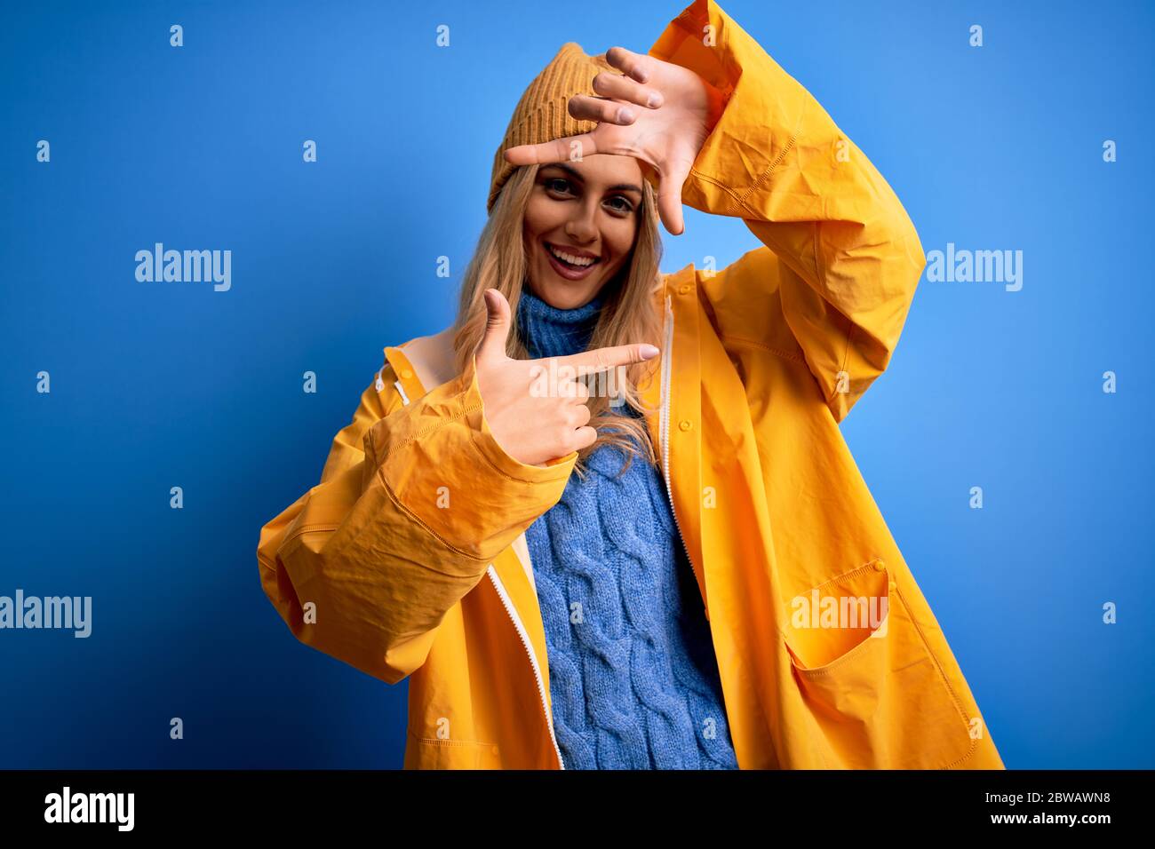 Young beautiful blonde woman wearing raincoat for rainy weather over ...