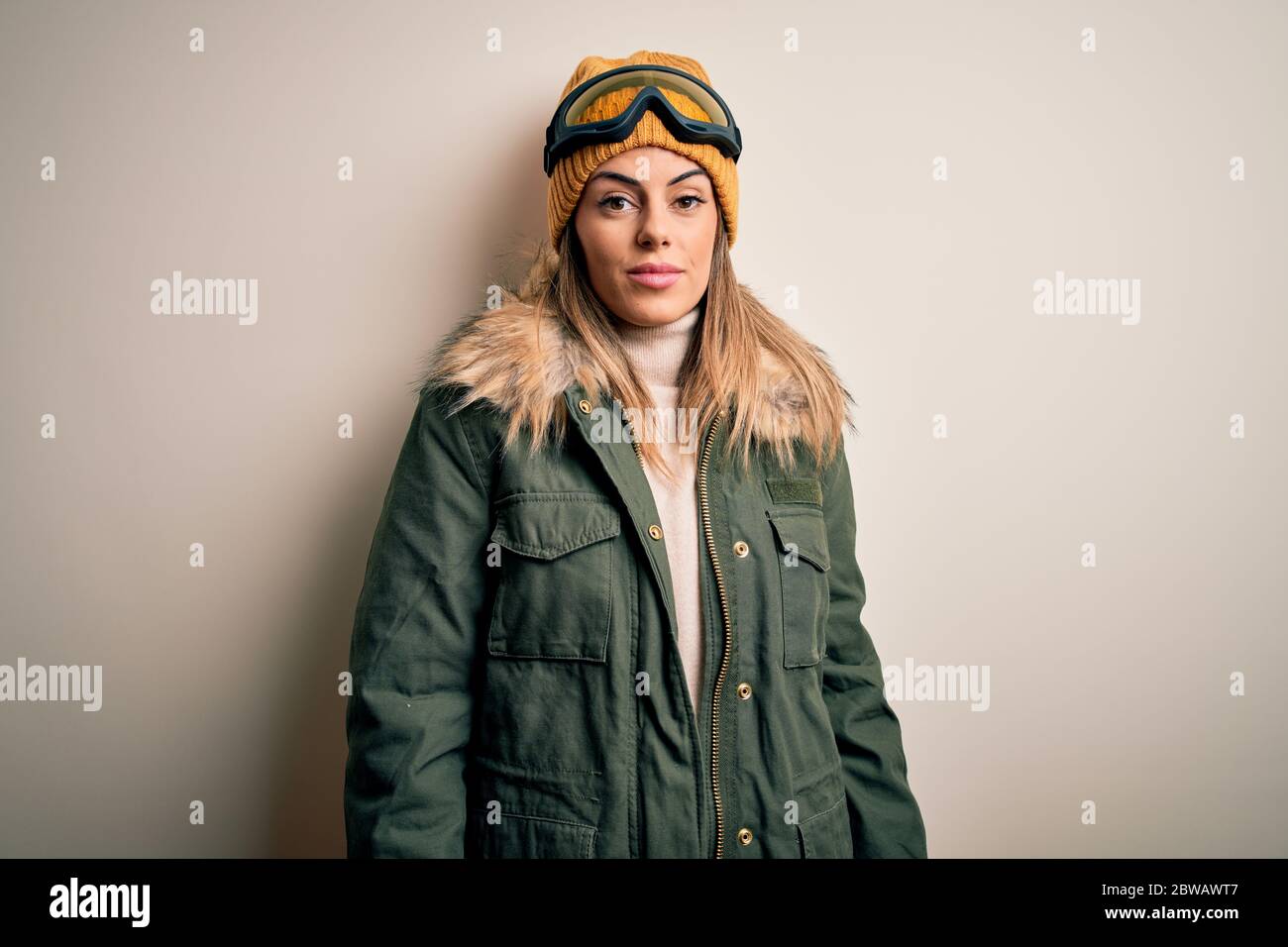 Young brunette skier woman wearing snow clothes and ski goggles over ...