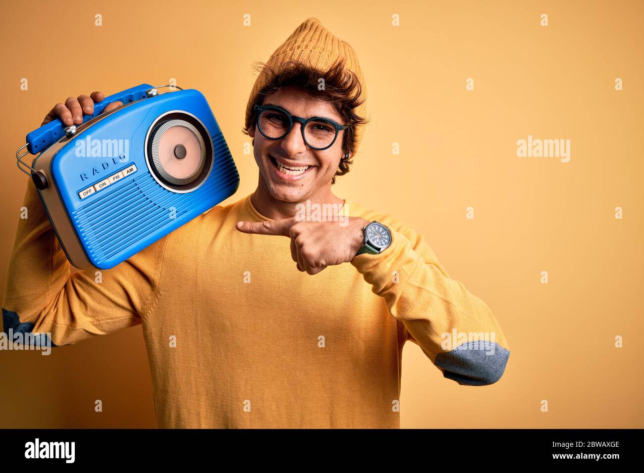 Young handsome man holding vintage radio standing over isolated yellow ...