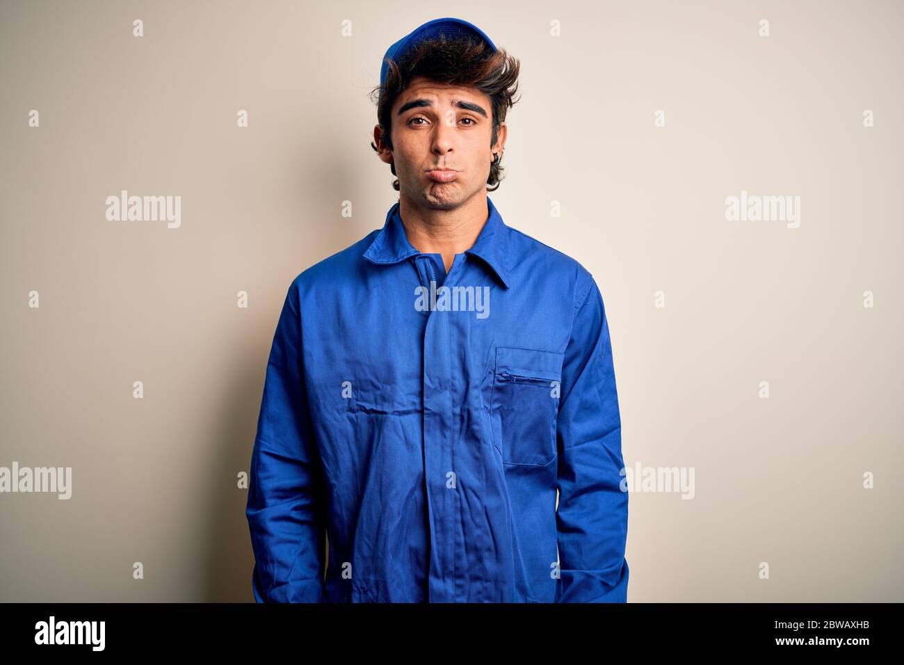 Young mechanic man wearing blue cap and uniform standing over isolated ...