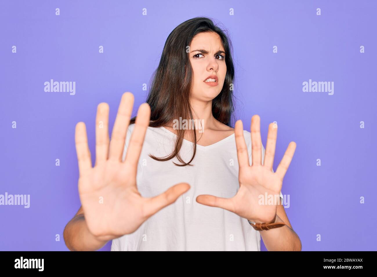 Young beautiful brunette woman wearing casual white t-shirt over purple ...