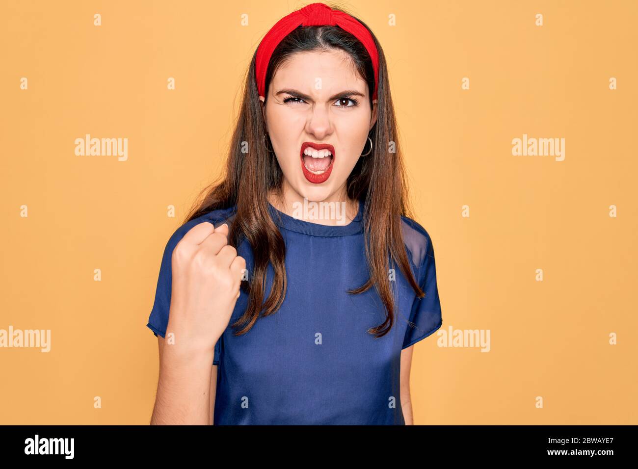 Young beautiful brunette woman wearing red lips over yellow background ...