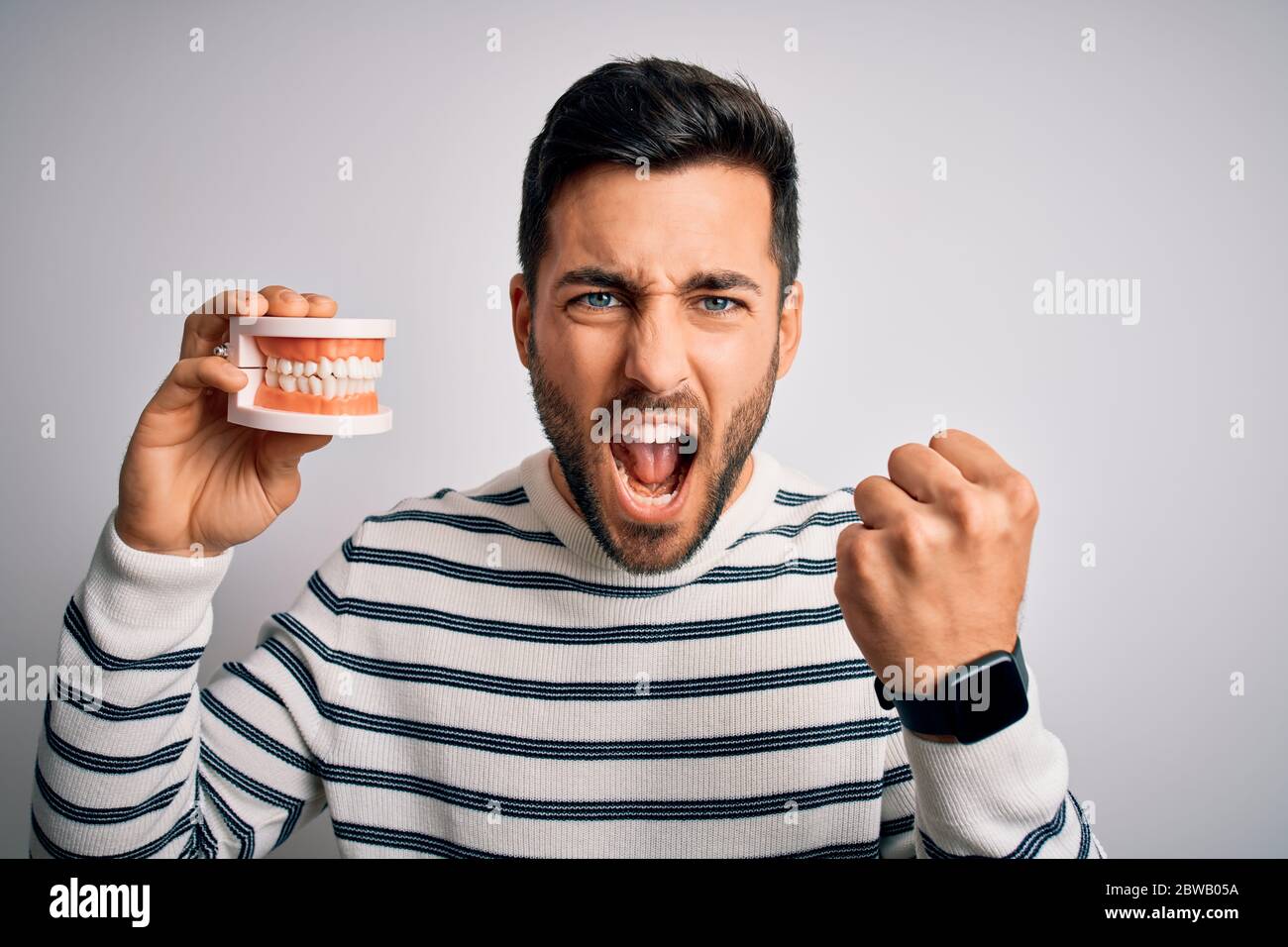 Young handsome man with beard holding plastic denture teeth over white ...